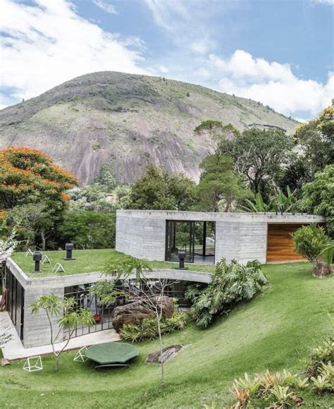 A House In The Middle Of A Lush Green Field With Mountains In The