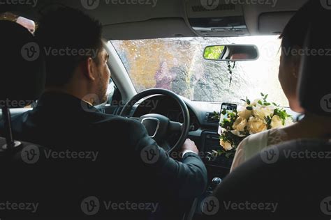 Interior Front Seat View Bride And Groom Sit In Car While Friends Spray Sparkling Wine On Car