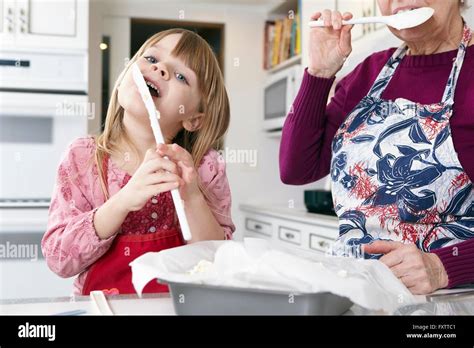 Mädchen und Oma lecken Kuchen mix vom Spatel am Küchentisch