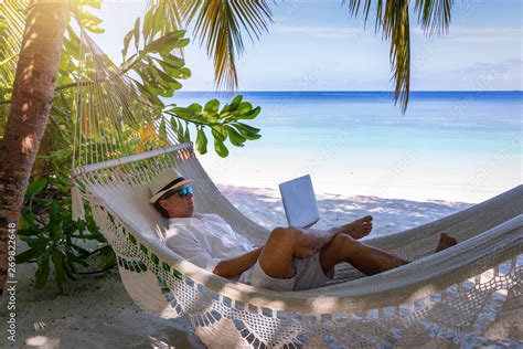 Arbeiten im Urlaub Mann mit Laptop auf Hängematte am tropischen Strand
