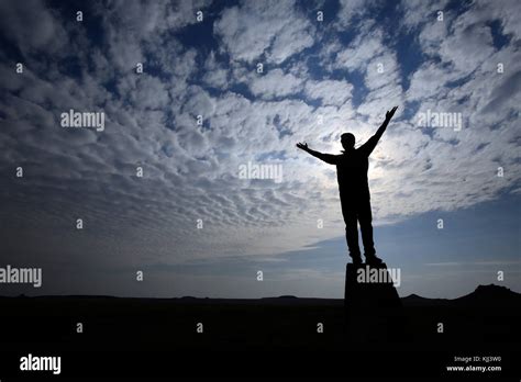 Man With Arms Raised Praying Against Cloudy Sky Silhouette Stock Photo