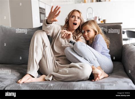 Image Of Two Scared Girls Sisters On Sofa At Home Indoors Watch Tv Horror Film Together Stock