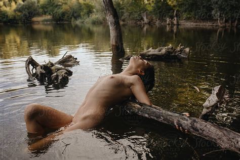 Naked Woman Leaning Over Tree In Lake Water Looking Up At The Sky By