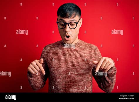 Young Handsome Hispanic Man Wearing Nerd Glasses Over Red Background Pointing Down With Fingers