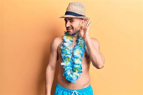 年轻英俊的秃头男子光着膀子穿着泳装和夏威夷花环微笑着用手捂着耳朵听和谣言或八卦高清图片下载 正版图片503852948 摄图网