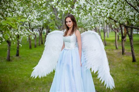 Woman In A White Corset And A Blue Puffy Dress With Large White Angel Wings Behind Her Back