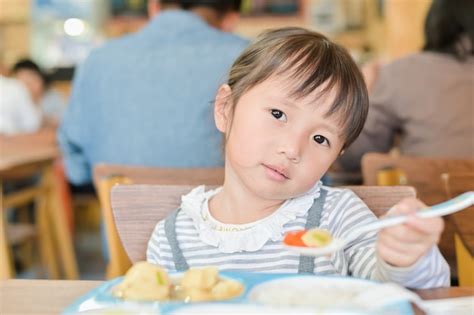 Pequeña niña asiática con cara infeliz mientras almuerza en la mesa en