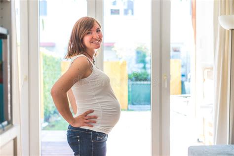 Happy Pregnant Mother In Blue Jeans Is Hugging Her Naked Tummy Close