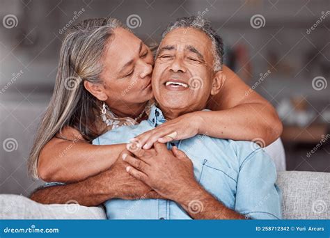 Happy Senior Couple Hug In Home Retirement Lifestyle Together In Mexico And Relax On Sofa