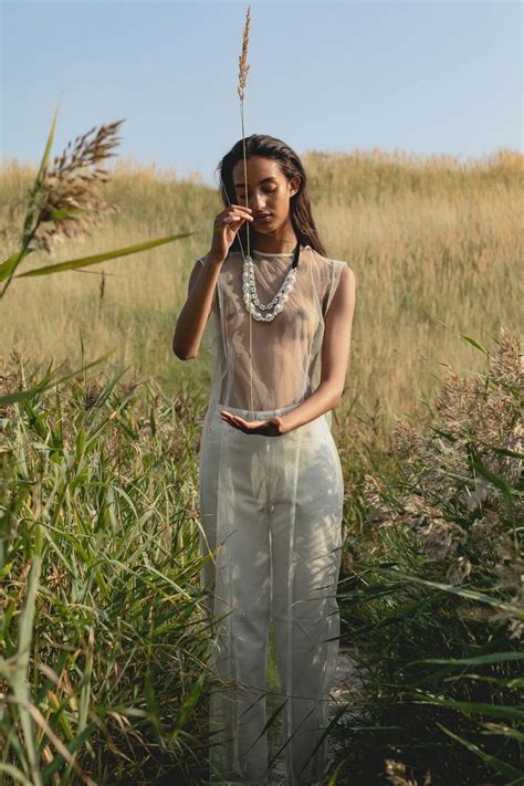 A Woman Standing In The Middle Of A Field Holding A Plant Up To Her Face