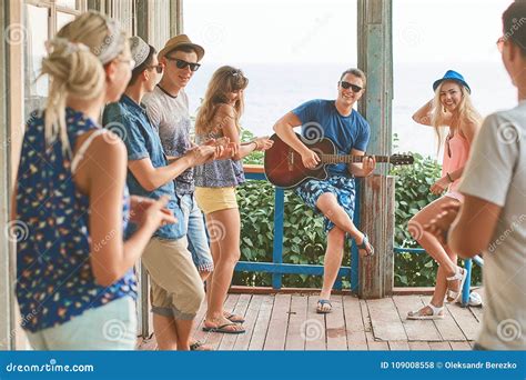 Friends Hanging Out On Vacation At An Old Wooden Cabin Porch By The Sea While One Of Them Is