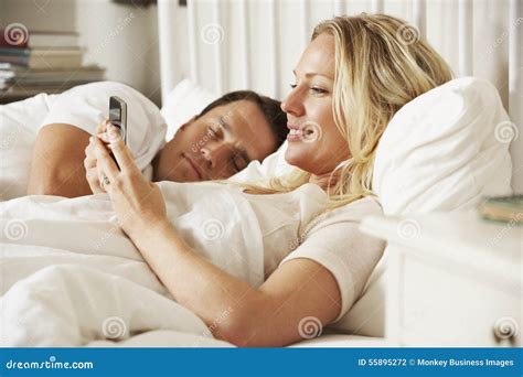 Woman Using Mobile Phone In Bed Whilst Husband Sleeps Stock Photo