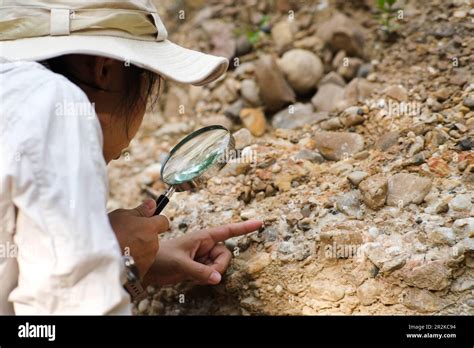 Female Geologist Using Magnifying Glass To Examine And Analyze Rock