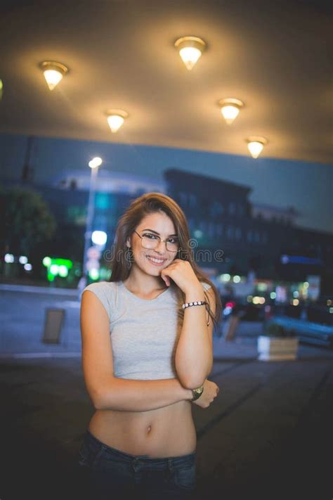 Smiling Brunette Girl With Eyeglasses Standing Outside In A Bright City Wearing A Crop Top Stock