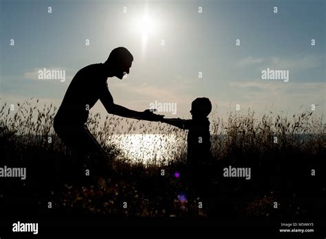 Silhouettes Of Father And Son Hold Hands And Look At Each Other Against