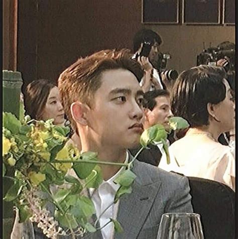 A Man In A Suit Sitting At A Table With Flowers And Wine Glasses On It
