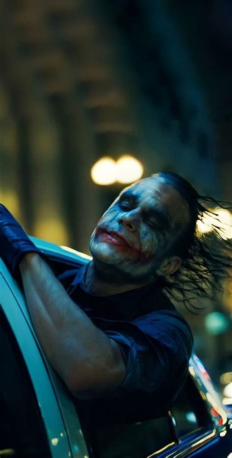 A Man With His Face Painted As The Joker Leaning Out Of A Car Window At