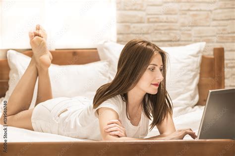 Expressive Woman Lying Down The Bed In Front Of Her Laptop With Her Legs Raised Slightly