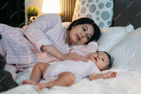 Premium Photo Selective Focus Asian First Time Mom Lying On Bed In Pajamas Is Looking At New