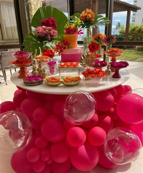 A Table Topped With Lots Of Pink And Orange Balloons Next To A Cake On