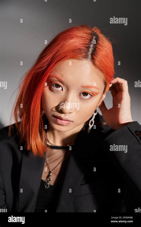 Portrait Of Young Asian Woman With Nose Piercing Looking At Camera And Adjusting Red Hair On