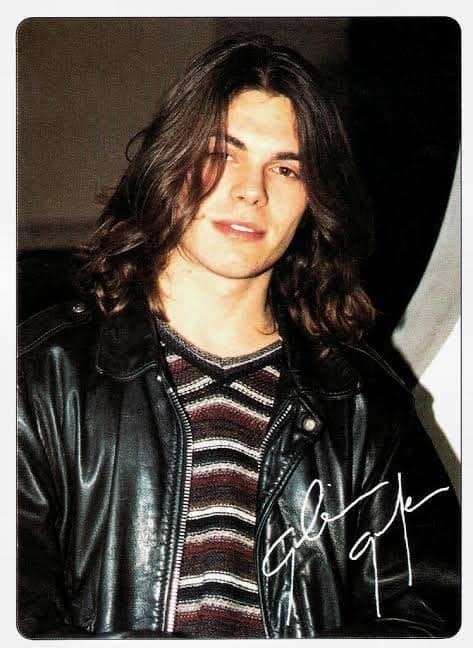 A Man With Long Hair Wearing A Black Leather Jacket And Striped Shirt