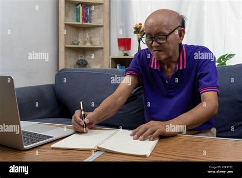 Asian Elderly Man Holding Pen Write Message Note And Computer Laptop On