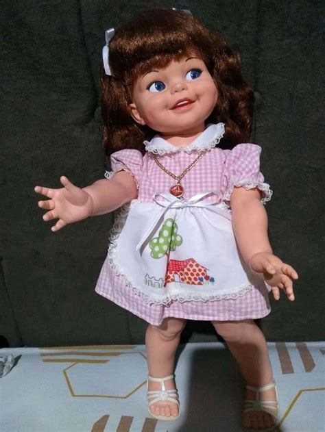 A Doll With Brown Hair And Blue Eyes Wearing A Pink Checkered Dress