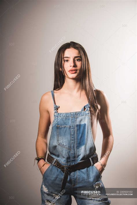 Sexy Mädchen im Jeansanzug über nacktem Körper posiert auf grauem