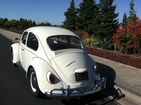 An Old White Car Is Parked On The Side Of The Road In Front Of Some Red