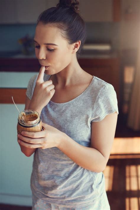 Peanut Butter On Her Fingertips An Attractive Young Woman Eating Peanut Butter While Standing