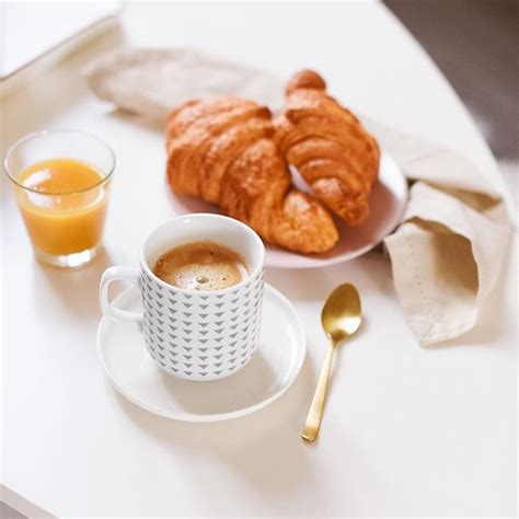 A Cup Of Coffee And Some Croissants On A White Table With Silverware