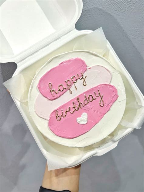 Someone Holding Up A Birthday Cake With Pink Frosting In A White Box