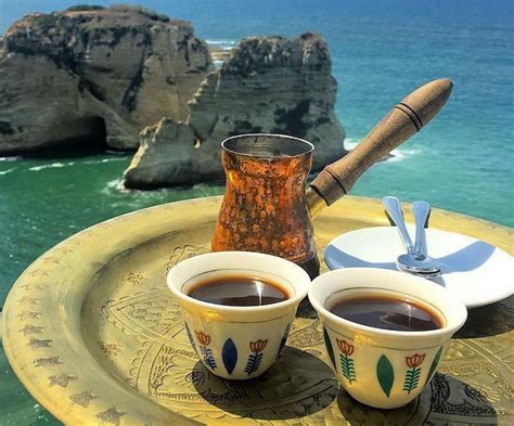Two Cups Of Coffee Sit On A Tray Overlooking The Ocean And Rocks In The
