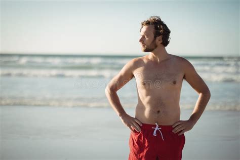 Thoughtful Shirtless Man Standing With Hands On Hip At Beach Stock