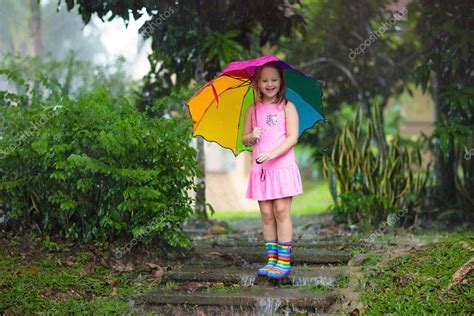 El chico jugando bajo la lluvia Los niños con paraguas y botas de