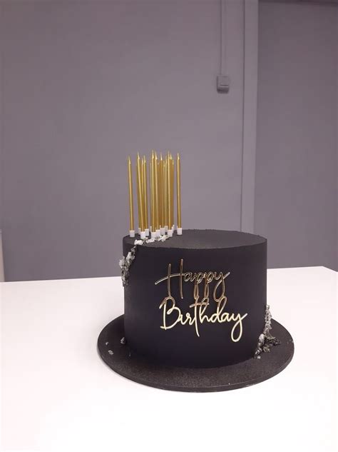 A Black And Gold Birthday Cake Sitting On Top Of A White Table With