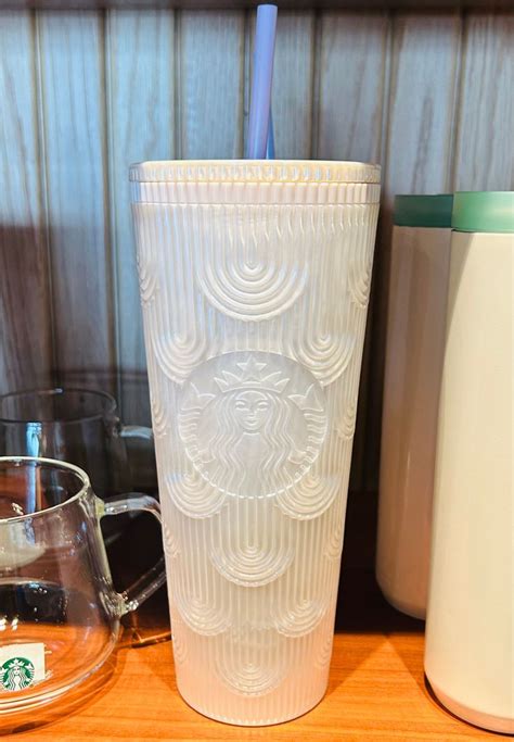 A Starbucks Cup With A Straw In It Sitting On A Counter Next To A Pitcher