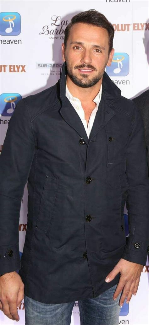 Two Men Standing Next To Each Other In Front Of A Red Carpet And White Wall