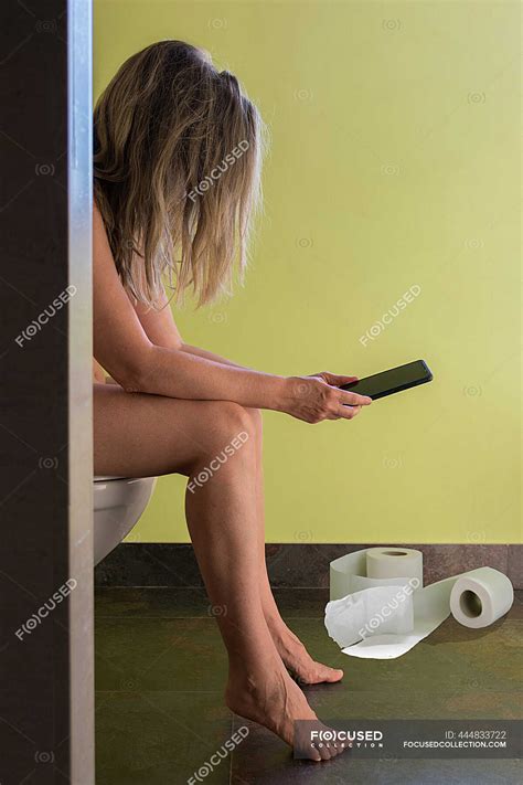 Blonde femme nue sur les toilettes regarder téléphone alors qu elle