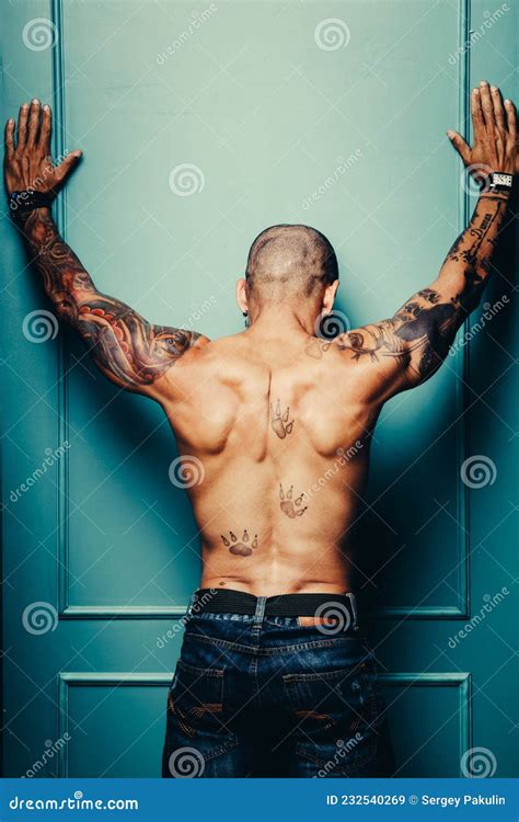 An African American With A Naked Muscular Body In Tattoos Stands Facing