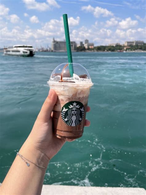 Someone Holding Up A Starbucks Drink In Front Of The Water