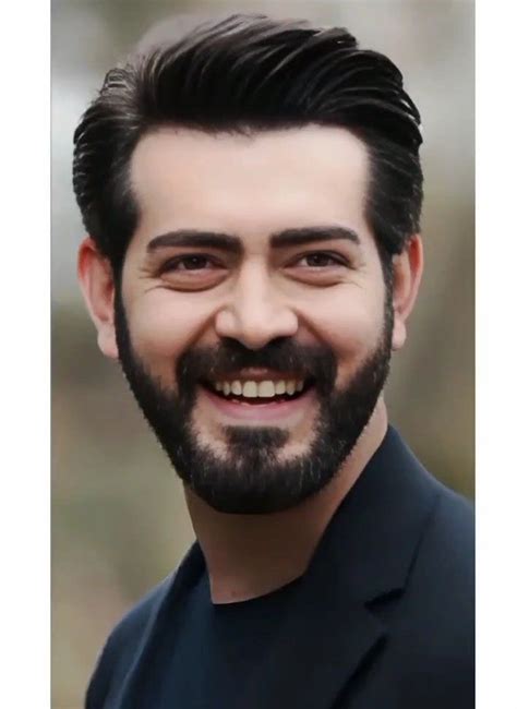 A Man With A Beard Smiling And Wearing A Black Suit Jacket In Front Of