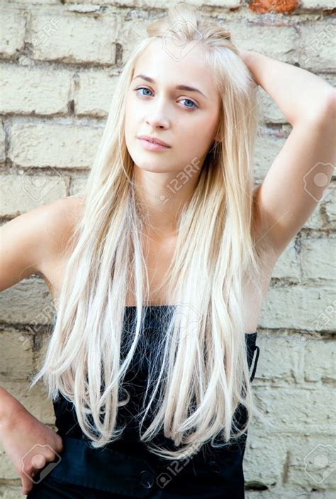 A Beautiful Blonde Woman With Long Hair Posing In Front Of A Brick Wall