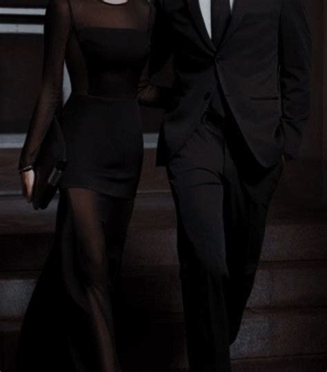 The Man And Woman Are Walking Down The Stairs In Black Dresses One Is