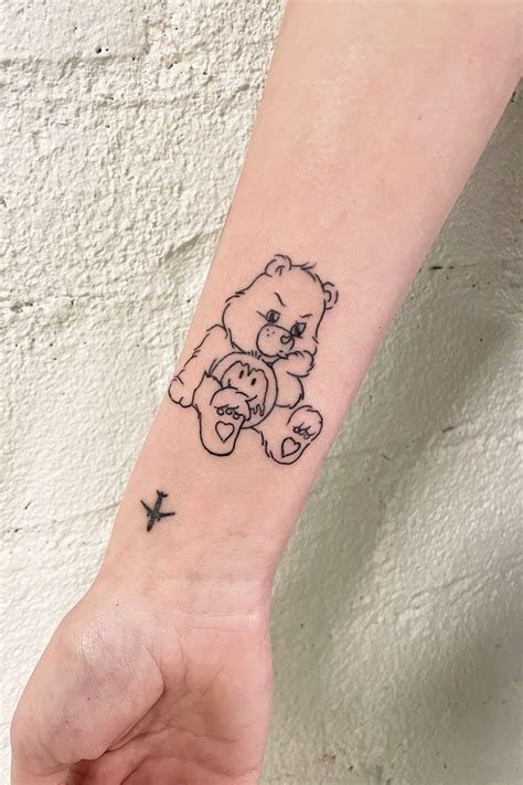A Small Tattoo On The Wrist Of A Person With A Teddy Bear Holding A Bird