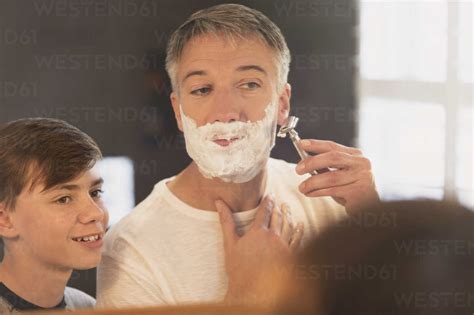 Son Watching Father Shave Face In Bathroom Mirror Stock Photo