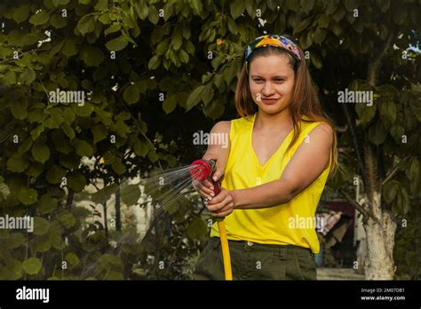 Young Pretty Girl Having Fun In The Garden Watering Plants With A Hose Smiling While Taking A