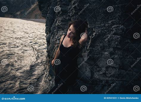 Seductive Girl In The Black Dress Standing Leaning Against The Rock