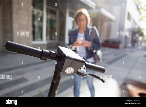 Woman Approaching Electric Scooter Rental On City Sidewalk Stock Photo